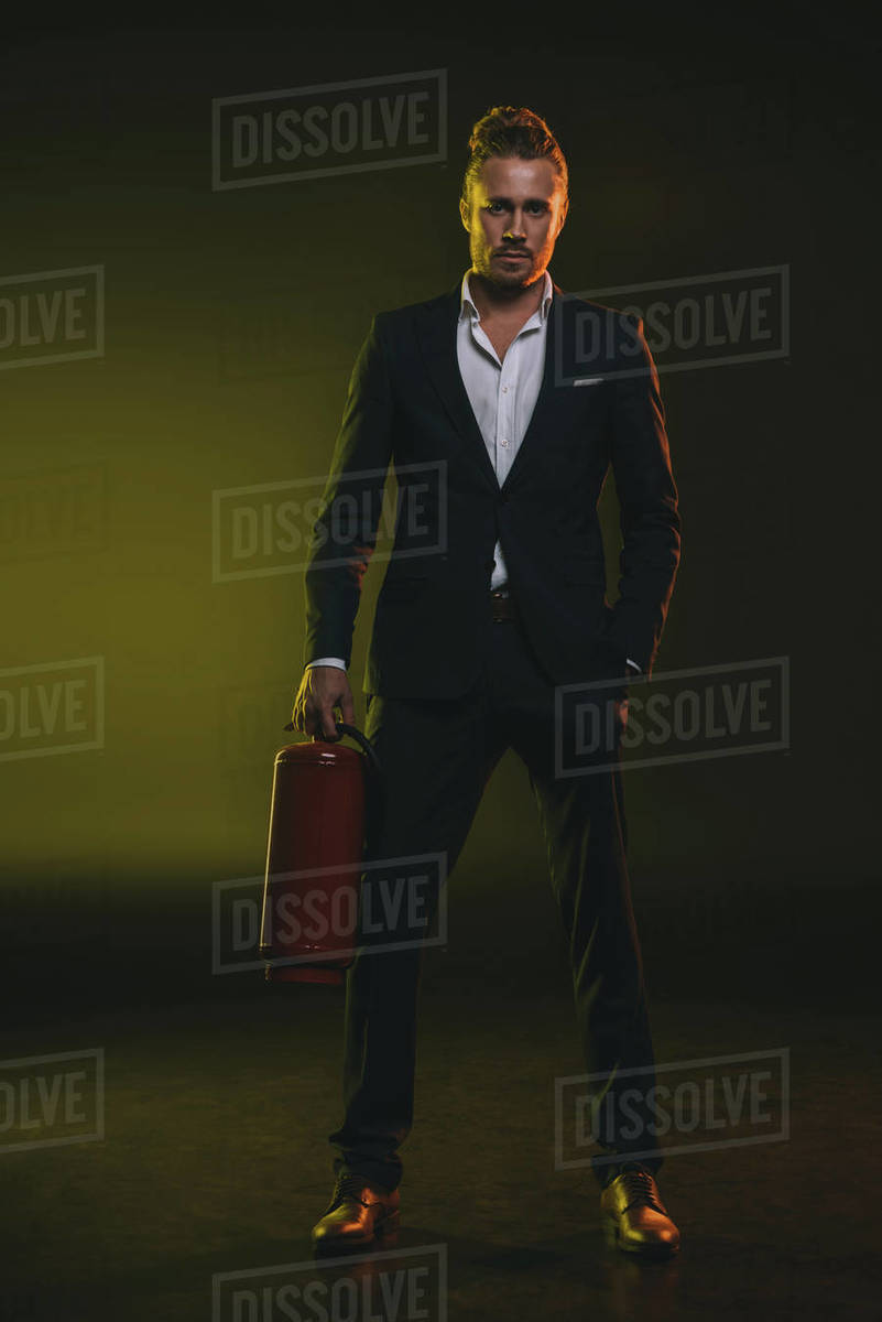 Young stylish man in tuxedo standing and holding fire extinguisher ...