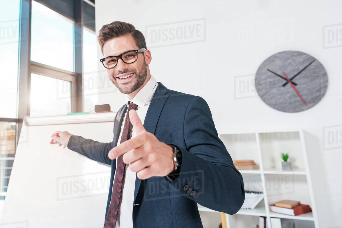 Cheerful young businessman pointing with finger and smiling at camera ...