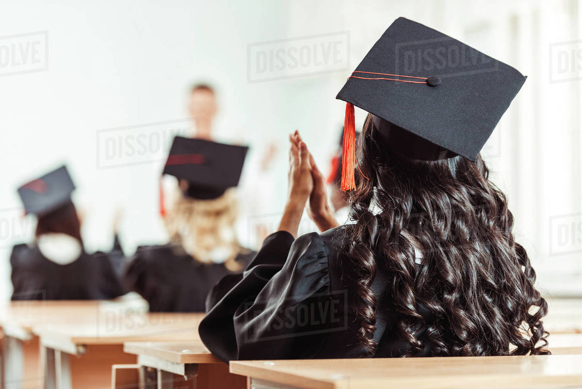 back view of student girl in graduation costume clapping hands while ...