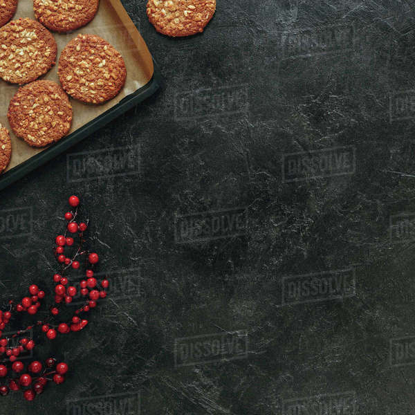 top view of freshly baked cookies on tray and red berries on black ...