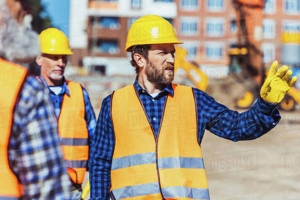 Builders discussing work while standing at construction site - Royalty ...