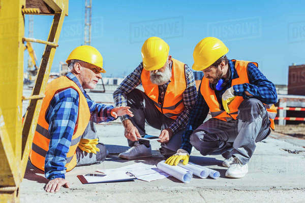 Three construction workers sitting on concrete at construction site ...