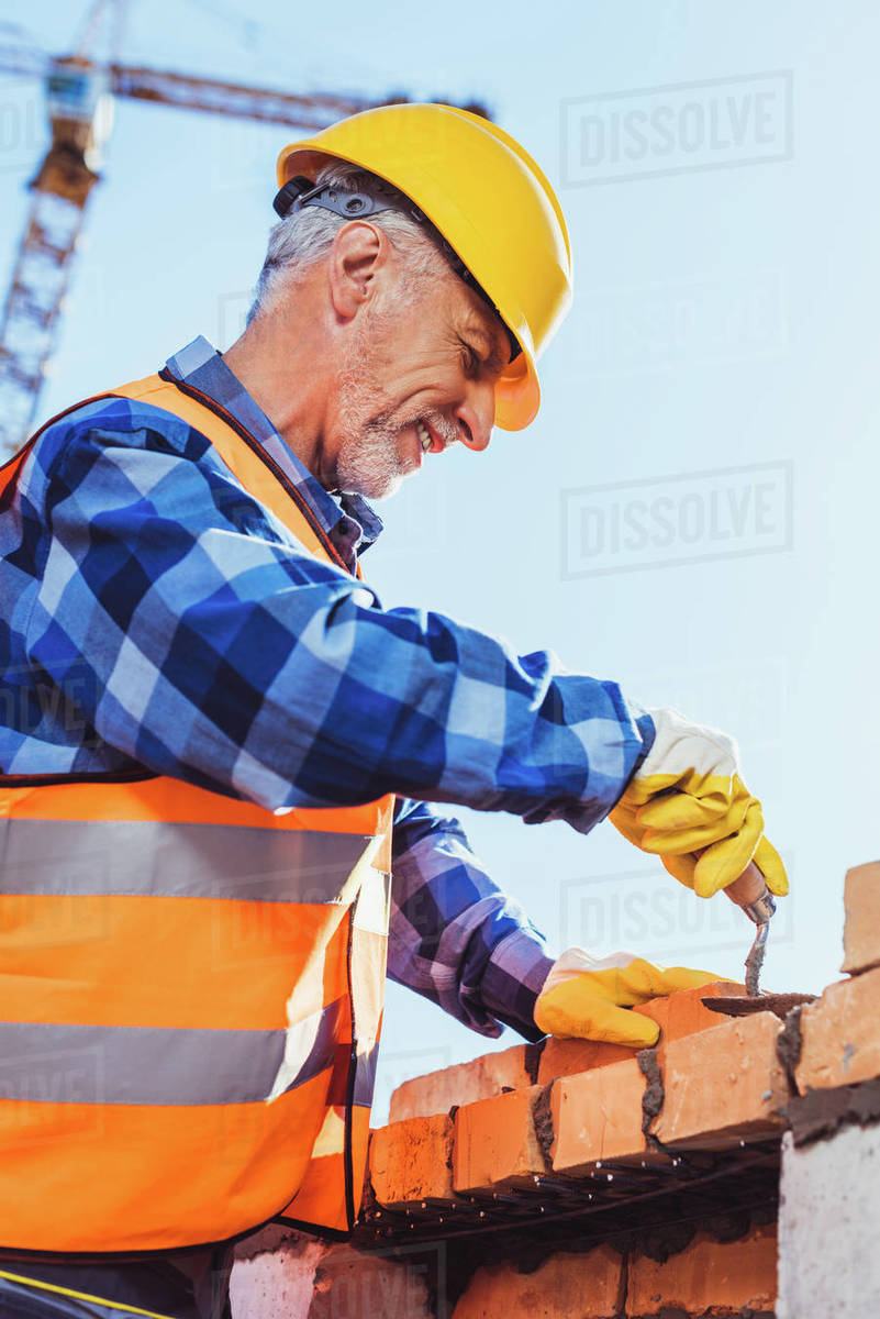 Construction worker in reflective vest and hardhat laying bricks using ...