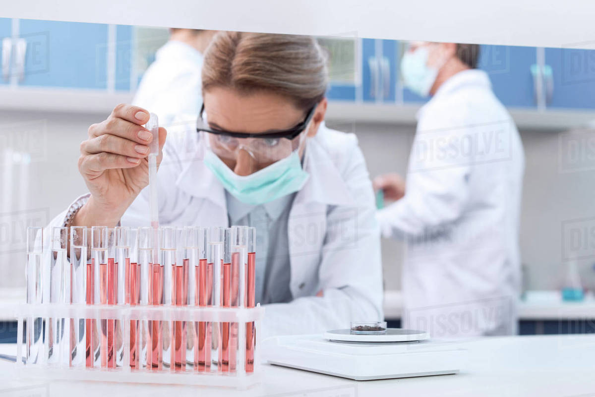 Professional scientist in sterile mask and protective glasses, making ...