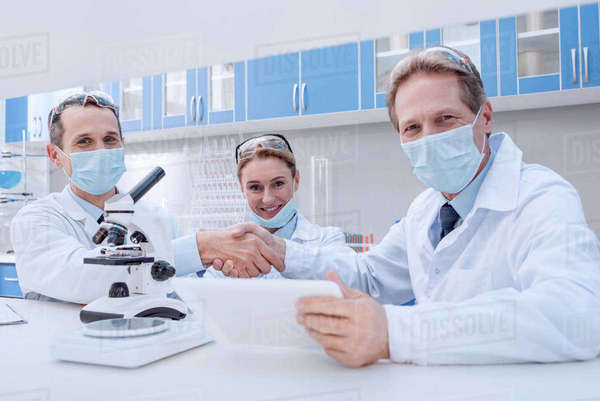 Doctors in lab coats and sterile masks, shaking hands and smiling ...