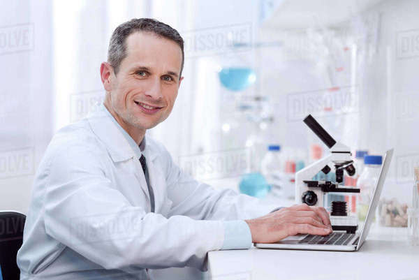 Side view of smiling professional chemist using laptop in laboratory ...