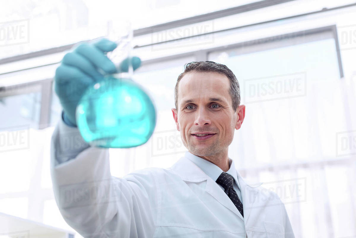Smiling scientist in lab coat holding test tube with blue liquid in ...