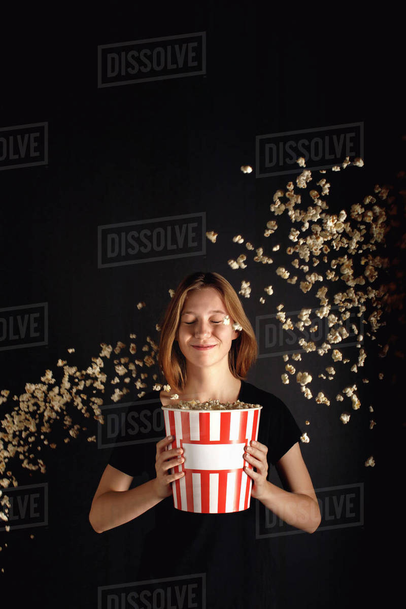 Woman with spilling popcorn and bucket in hands isolated on black ...
