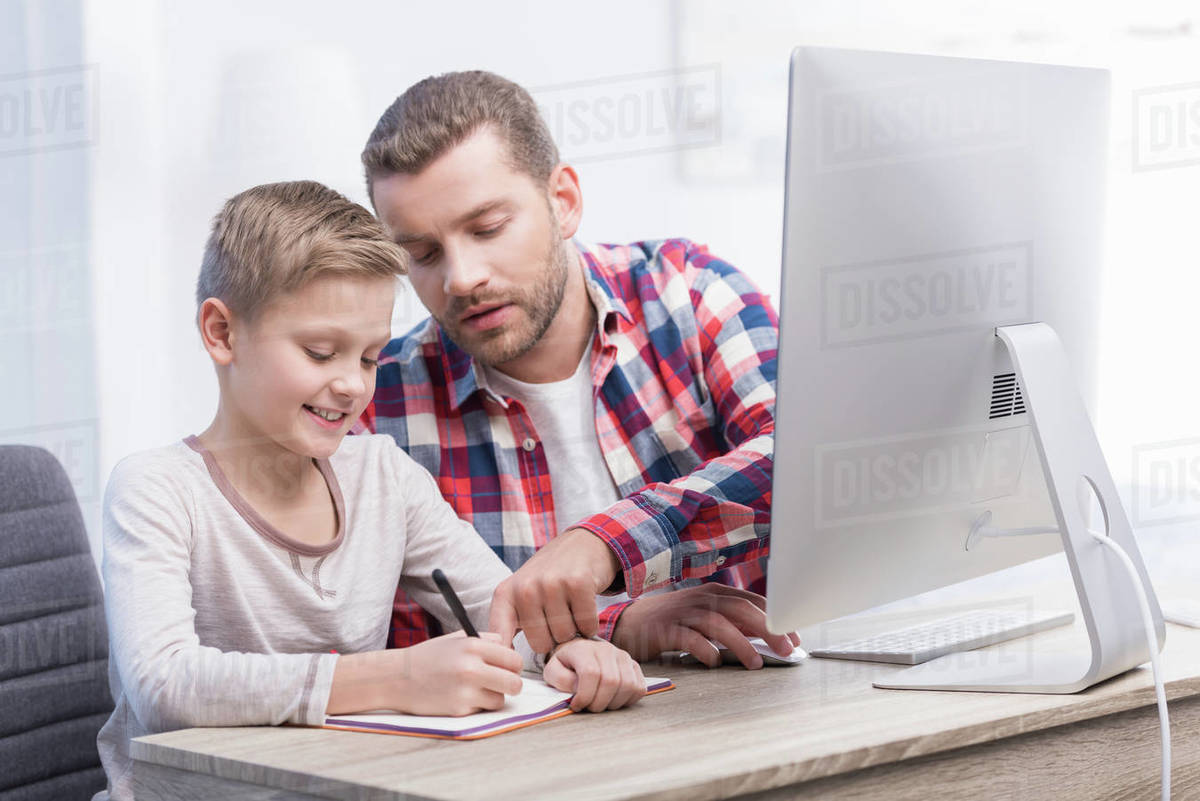 Father and son using desktop computer and taking notes together ...
