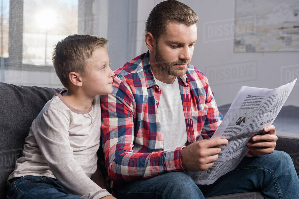Cute little boy looking at father reading newspaper at home - Royalty ...