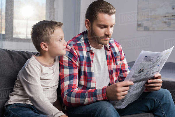 Cute little boy looking at father reading newspaper at home - Royalty ...