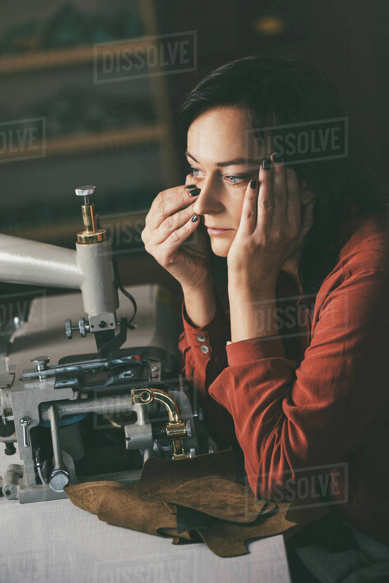 Pensive seamstress looking away while working with sewing machine and ...