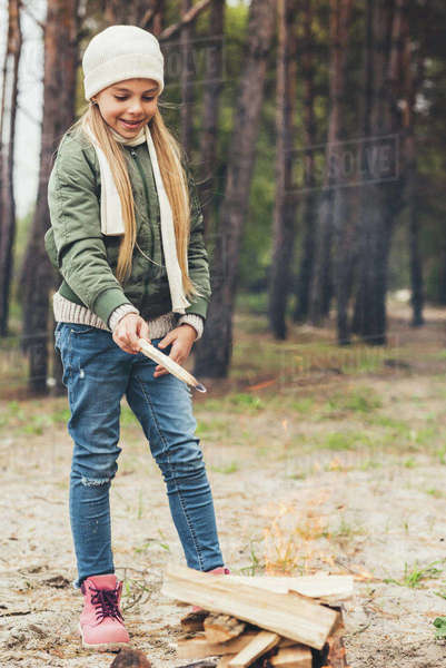 happy little girl adding wood to bonfire in forest - Royalty-free Stock ...