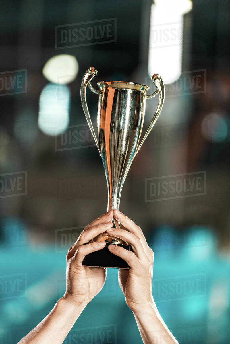 Cropped view of swimmer holding trophy cup at competition swimming pool ...
