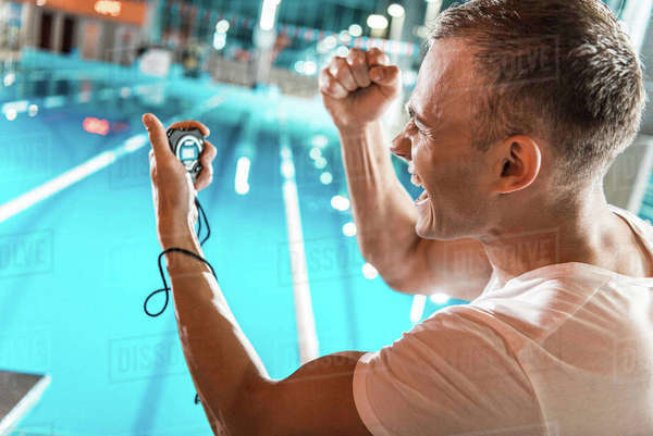 Excited swim trainer with stopwatch standing at competition swimming ...
