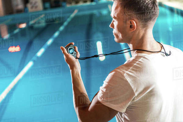 Handsome swim trainer with stopwatch standing at competition swimming ...