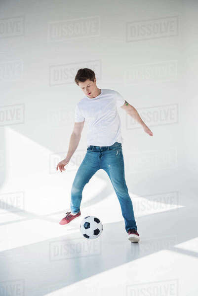 Full length view of young man playing with soccer ball on grey ...