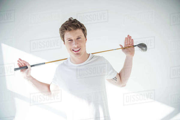 Handsome young man holding golf club and smiling at camera on grey ...