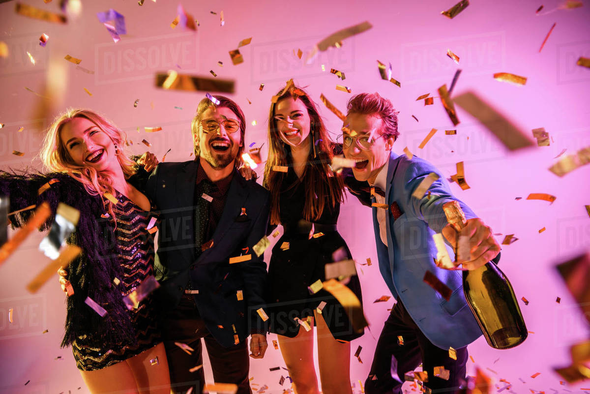 Excited friends with champagne bottle having fun on party with confetti ...