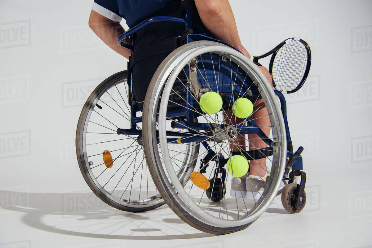 Cropped view of tennis player sitting in wheelchair with tennis racquet ...