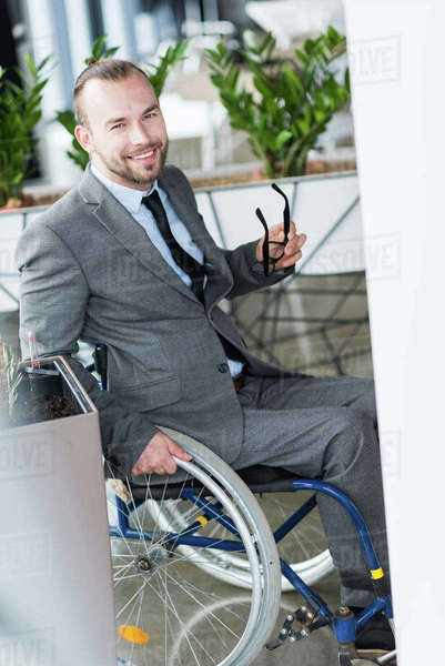 Smiling physically handicapped businessman holding glasses and looking ...