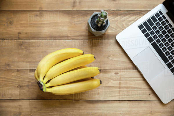 Top view of laptop and bunch of fresh ripe bananas on wooden table top ...