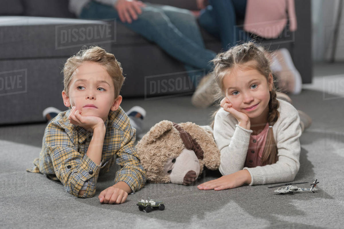 Two little children lying on floor in living room with toys and posing ...