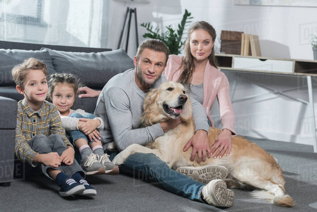 Family with two kids and dog sitting on floor in living room and ...
