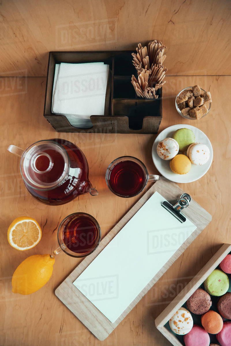 Top view of tea set with macarons and empty paper sheet on clipboard ...