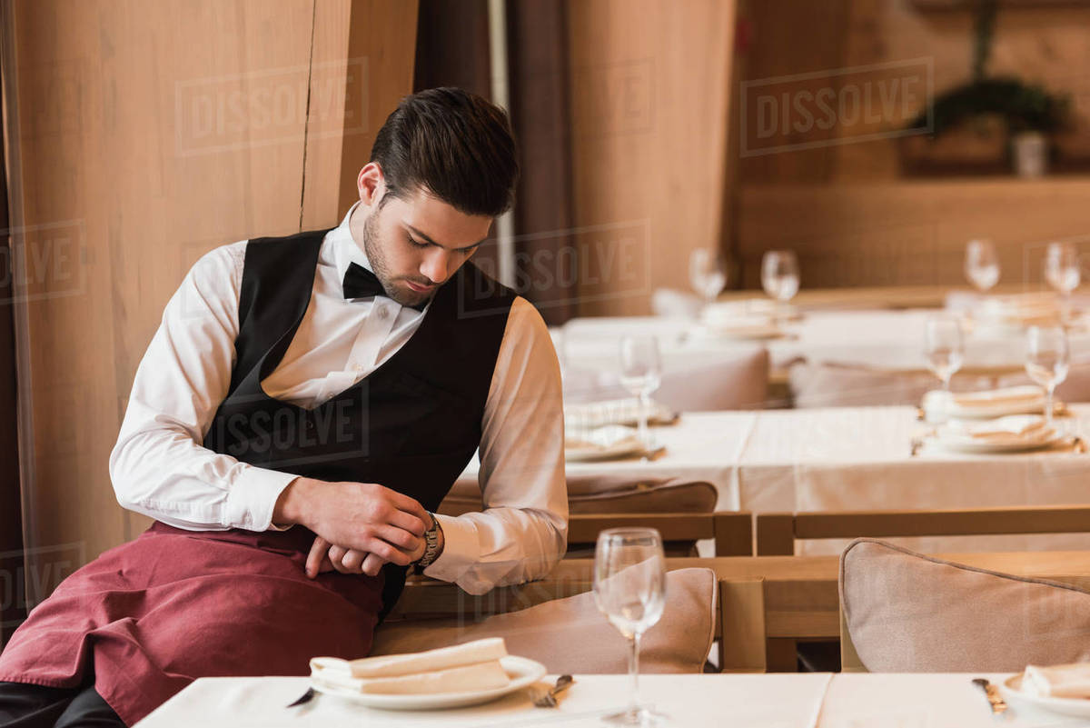 Waiter leaning on chair and looking at watch - Stock Photo - Dissolve
