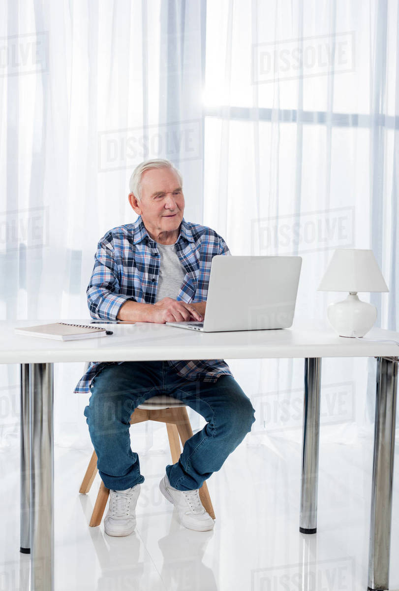senior man sitting at table and using laptop at home - Royalty-free ...