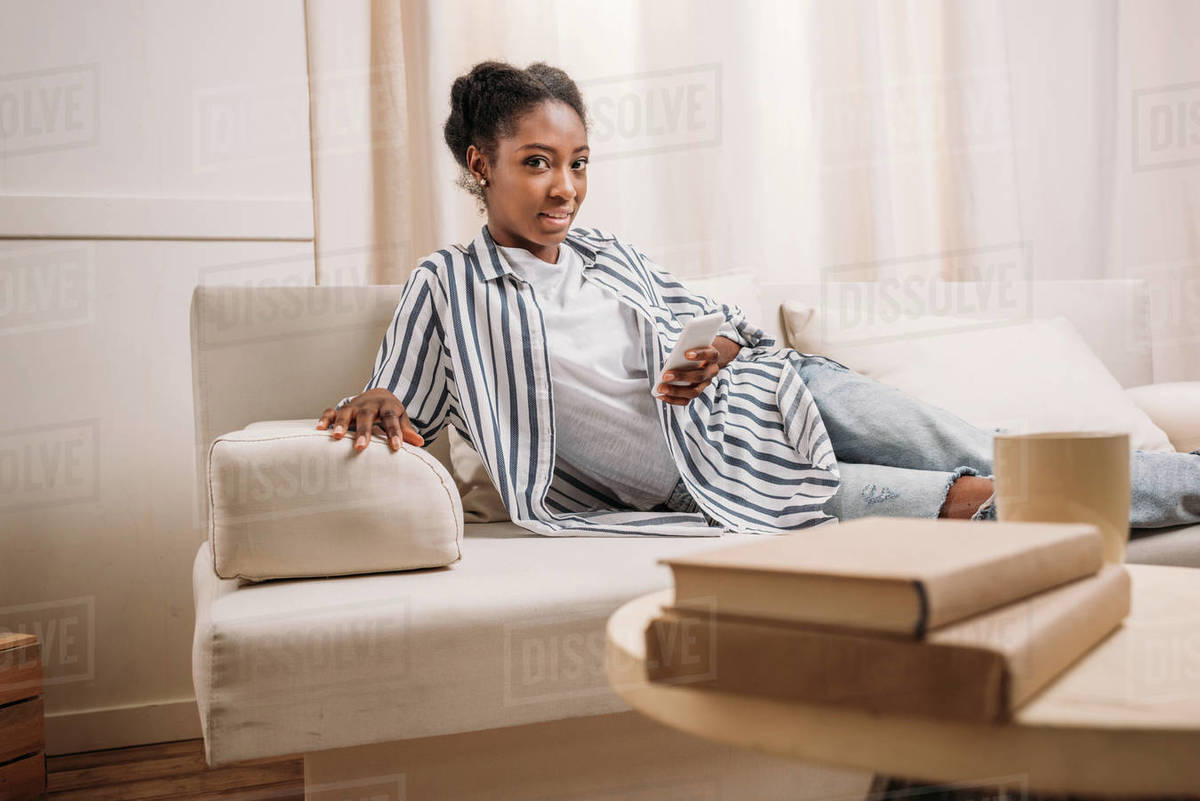 Pretty African American woman laying on couch and using smartphone at ...