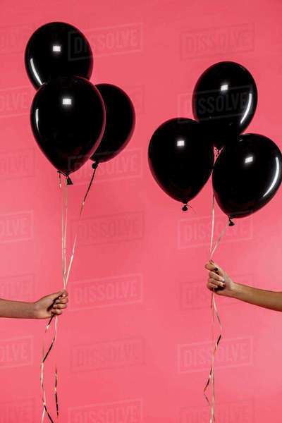 Cropped shot of human hands holding black balloons isolated on pink ...
