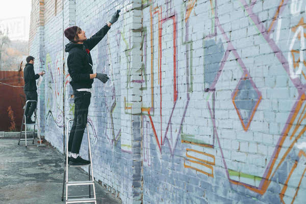 Street artists standing on ladders and painting colorful graffiti on ...