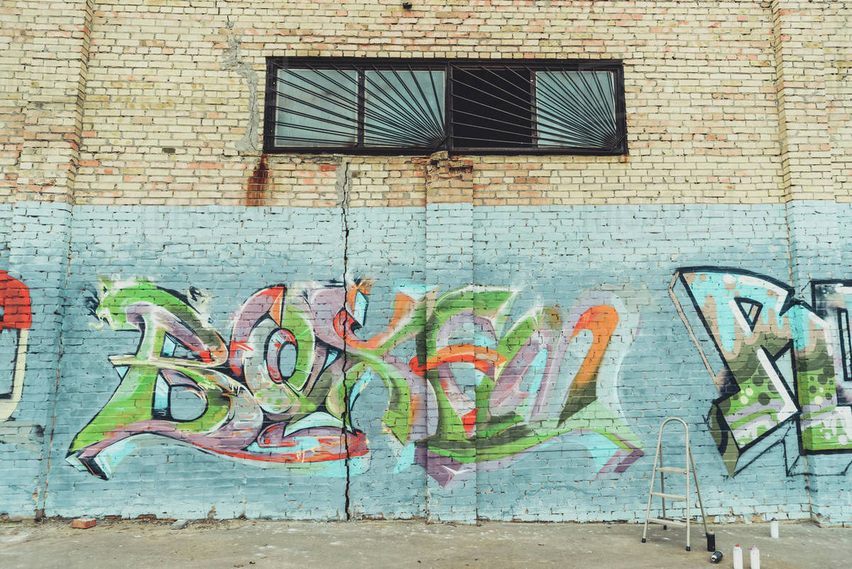 Cans with spray paint and ladder near colorful graffiti on wall of ...