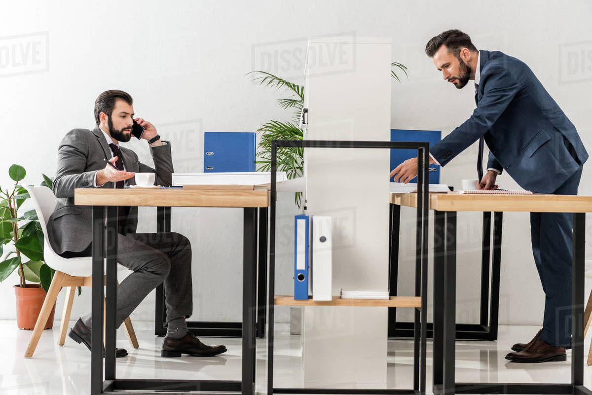 Side view of businessmen working at tables in office - Royalty-free ...