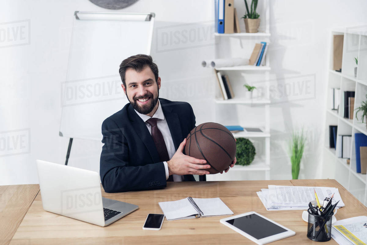 Portrait of young businessman with basketball ball at workplace in ...