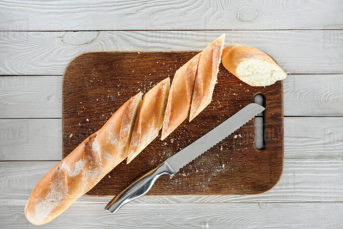 Top view of sliced homemade baguette and knife on wooden cutting board ...