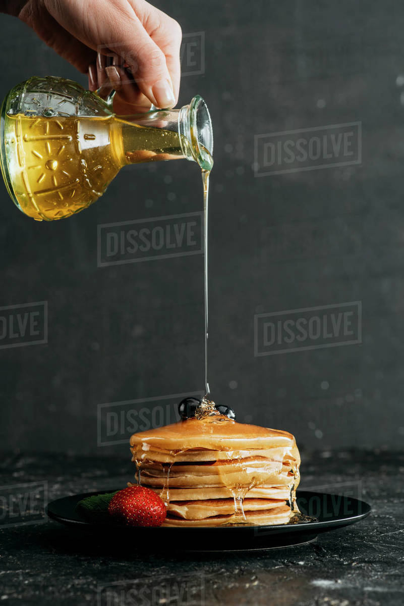 Cropped shot of woman pouring maple syrup onto stack of freshly baked ...