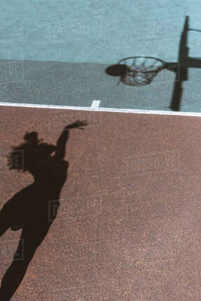 Shadows of female figure throwing ball into basket on ground of sports ...