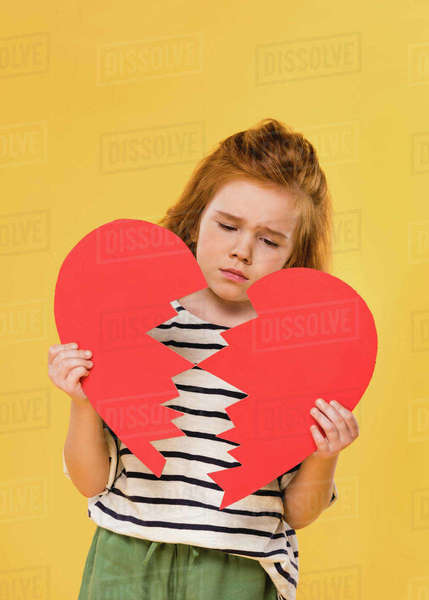 portrait of sad child with broken red paper heart isolated on yellow ...