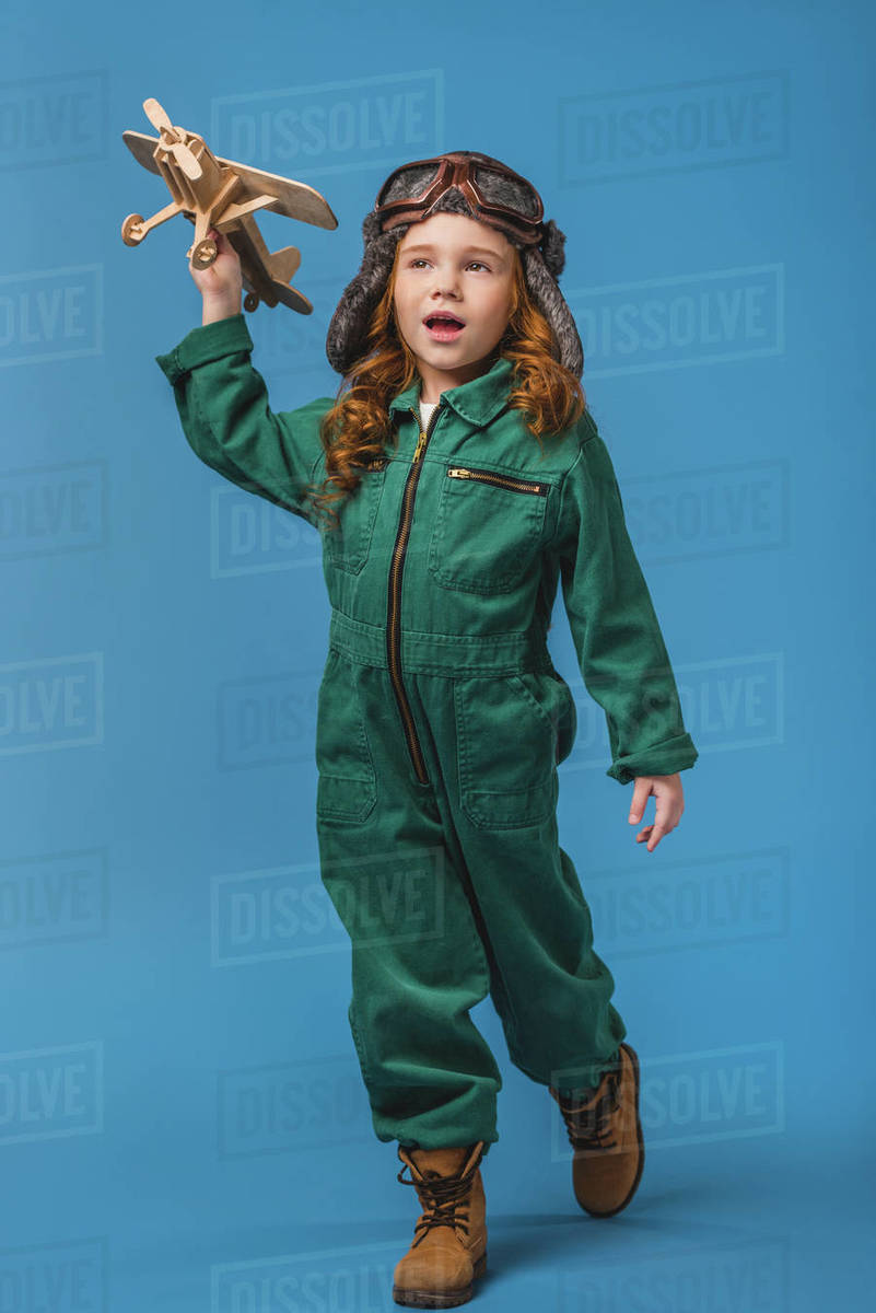 adorable child in pilot costume with wooden plane toy isolated on blue ...