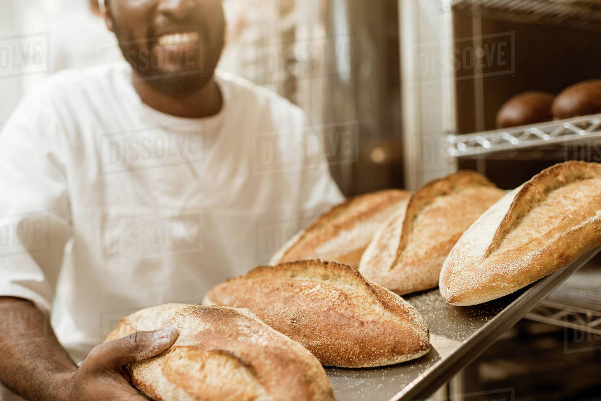 Cropped shot of smiling african american baker with tray of fresh ...