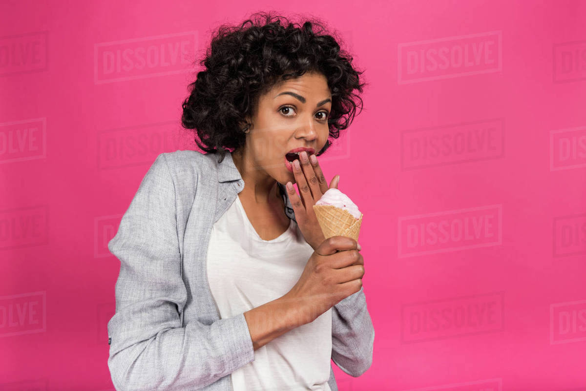 Surprised African American woman holding ice cream isolated on pink ...