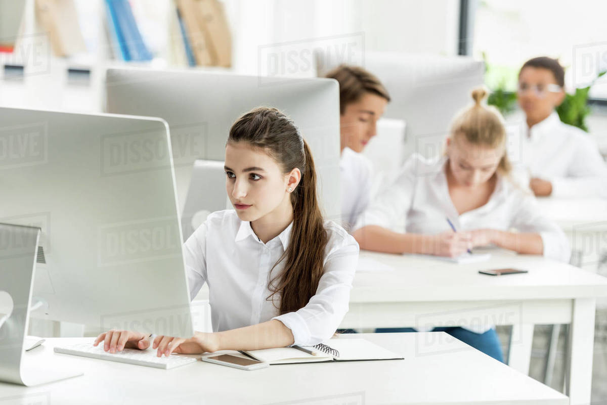 Portrait of focused teenage girl in white shirt working on computer ...