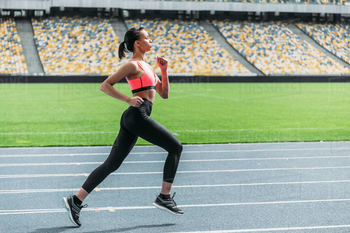 Side view of athletic young woman in sportswear sprinting on running ...
