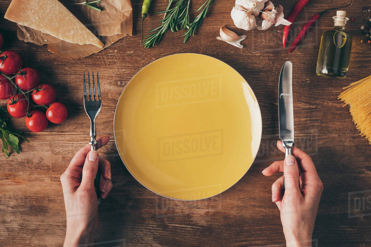 Cropped view of hands with knife and fork at plate with row pasta and ...