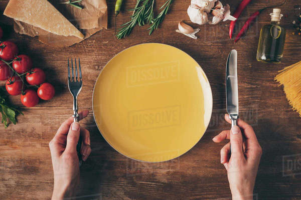 Cropped view of hands with knife and fork at plate with row pasta and ...