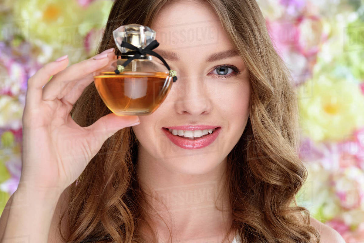 Close-up portrait of smiling young woman covering one eye with bottle ...