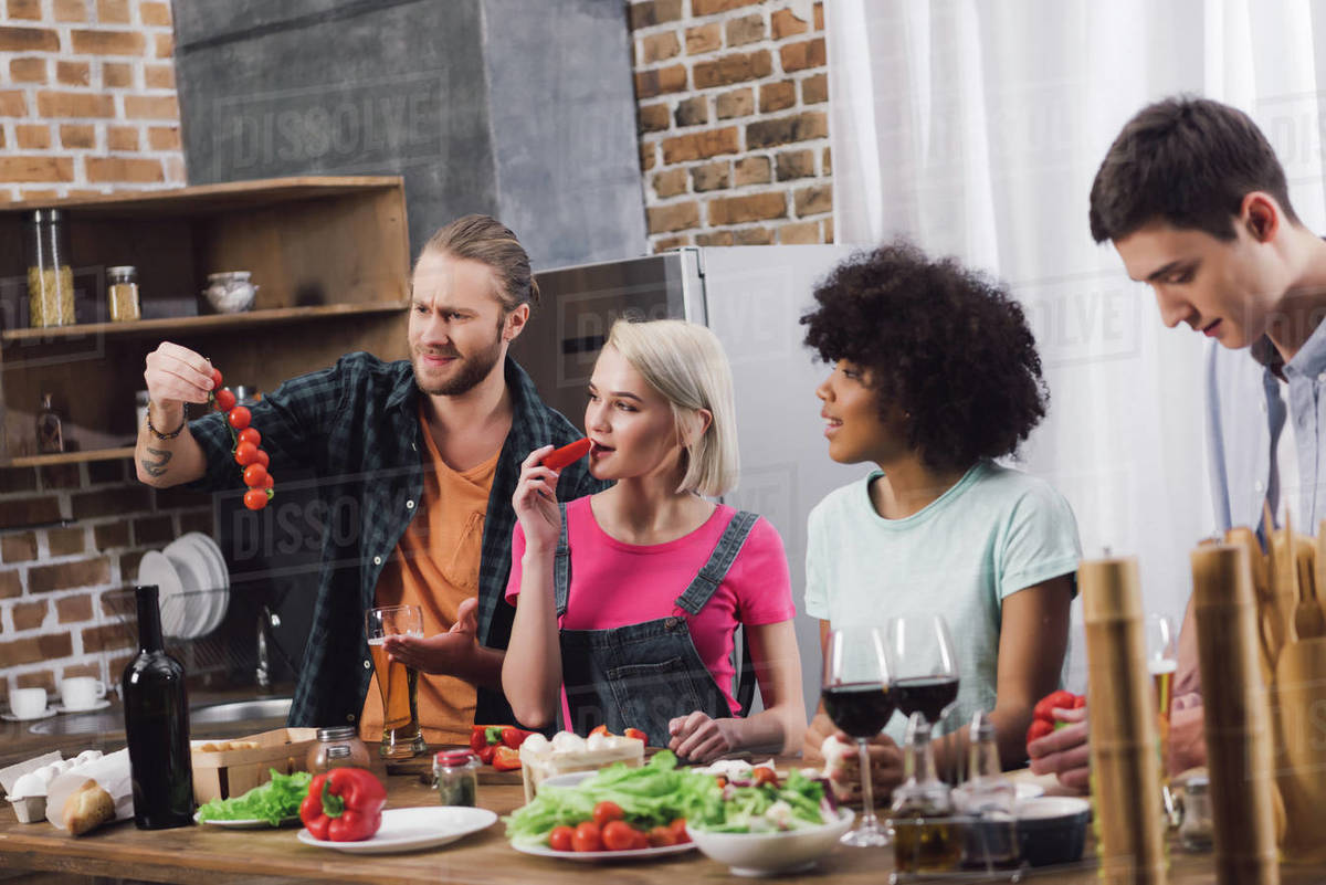 Multiethnic friends tasting some food while cooking in kitchen ...